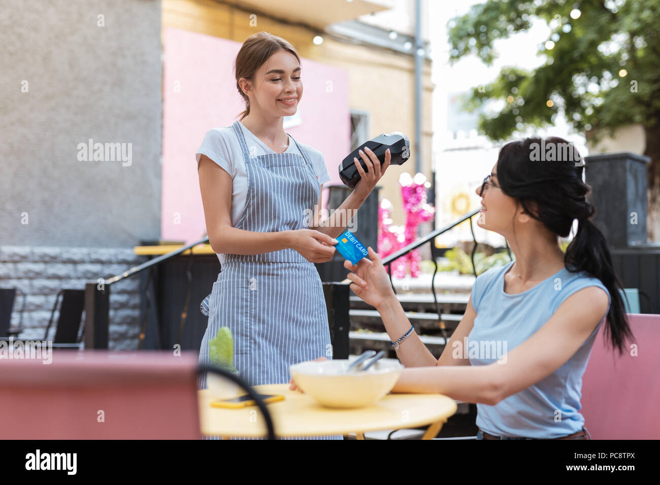 Bank card. Young pleasant waitress wearing striped apron receiving bank ...