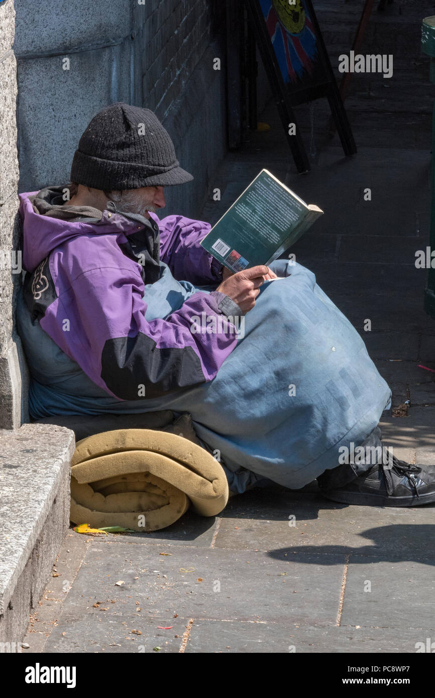a homeless person in central London reading a book to pass the time ...