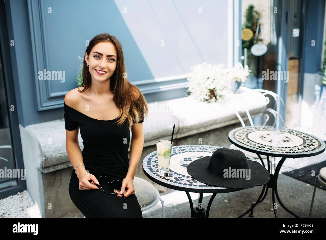 Young pretty girl sitting in a cafe on the street and drinking cooled ...