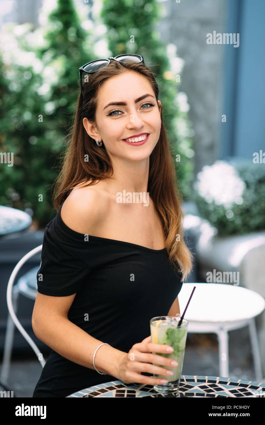 Young pretty girl sitting in a cafe on the street and drinking cooled ...