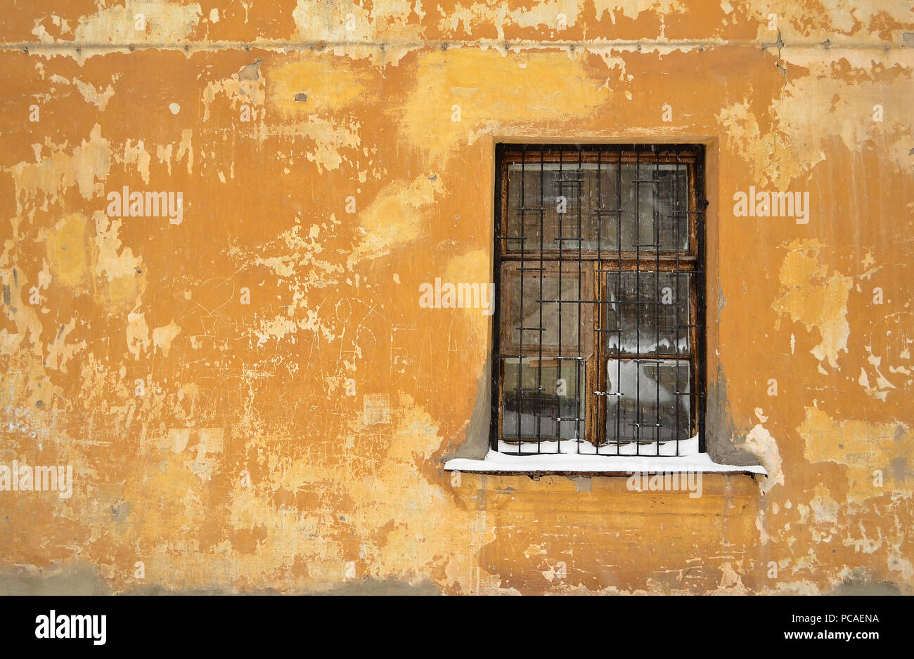 A barred window on the old yellow wall with a snow-covered window sill ...