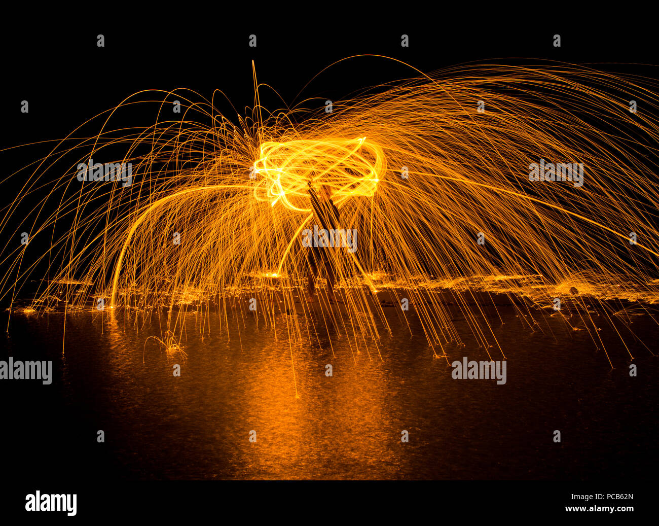 Boy twirling a lasso made of flames by a river, long exposure at night ...