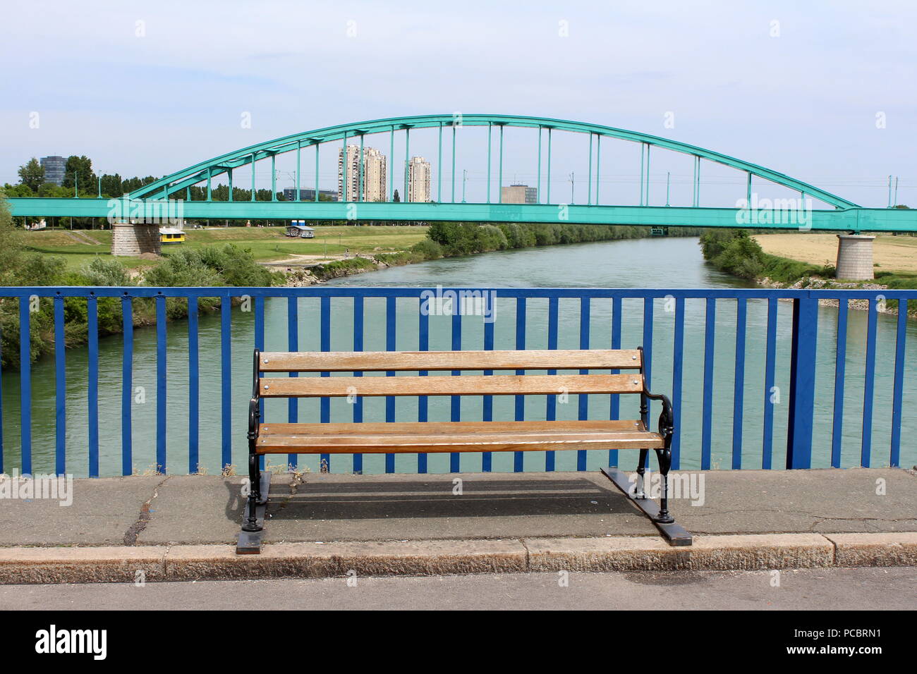 Public wooden bench with wrought iron legs mounted on asphalt road with ...