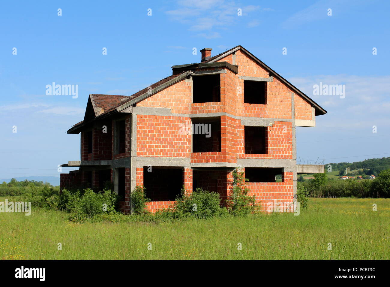 Unfinished brick family suburban house without doors or windows with roof tiles falling apart ...
