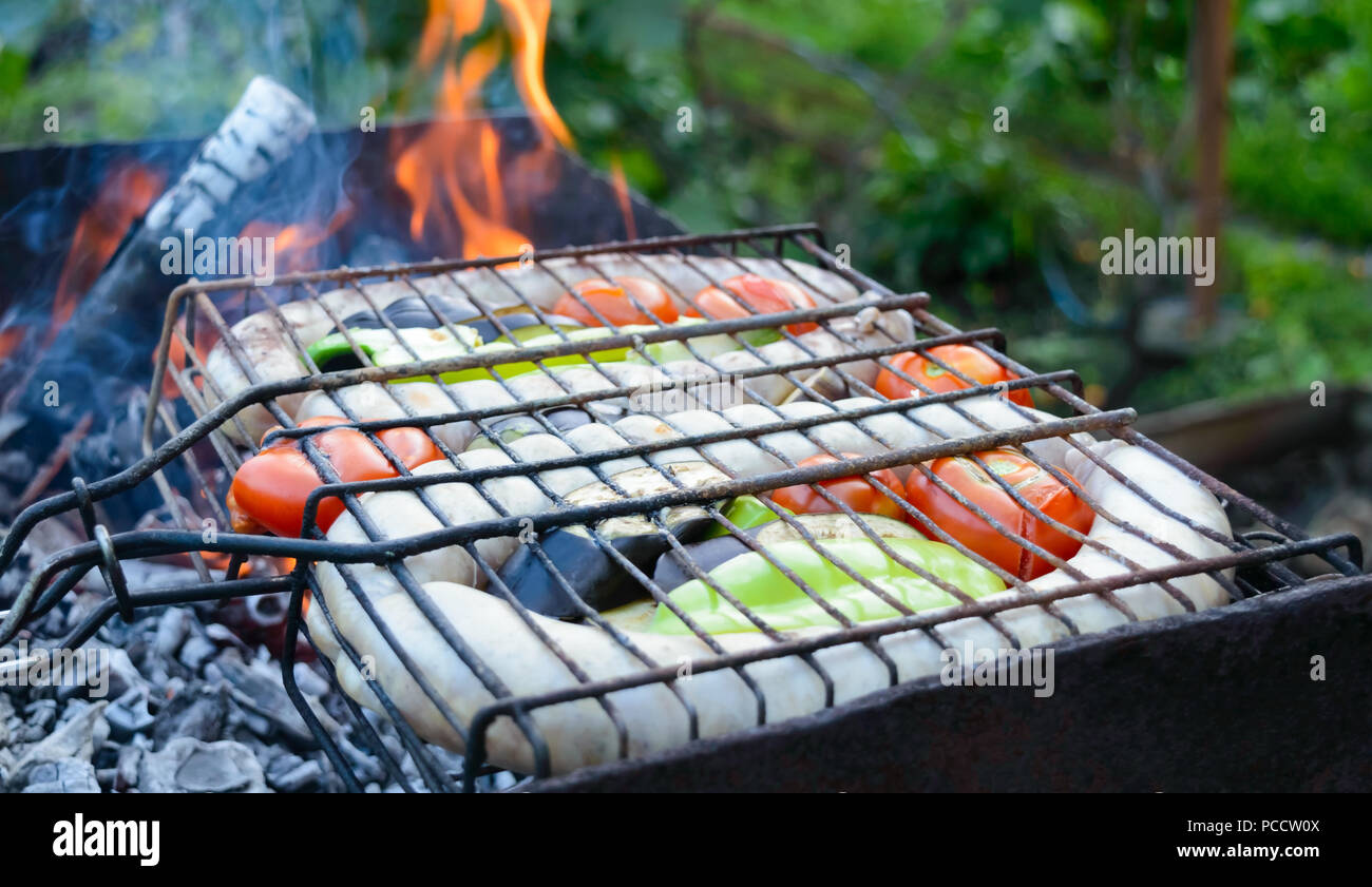 Pork sausages with vegetables are grilled on fire. Cooking dinner ...