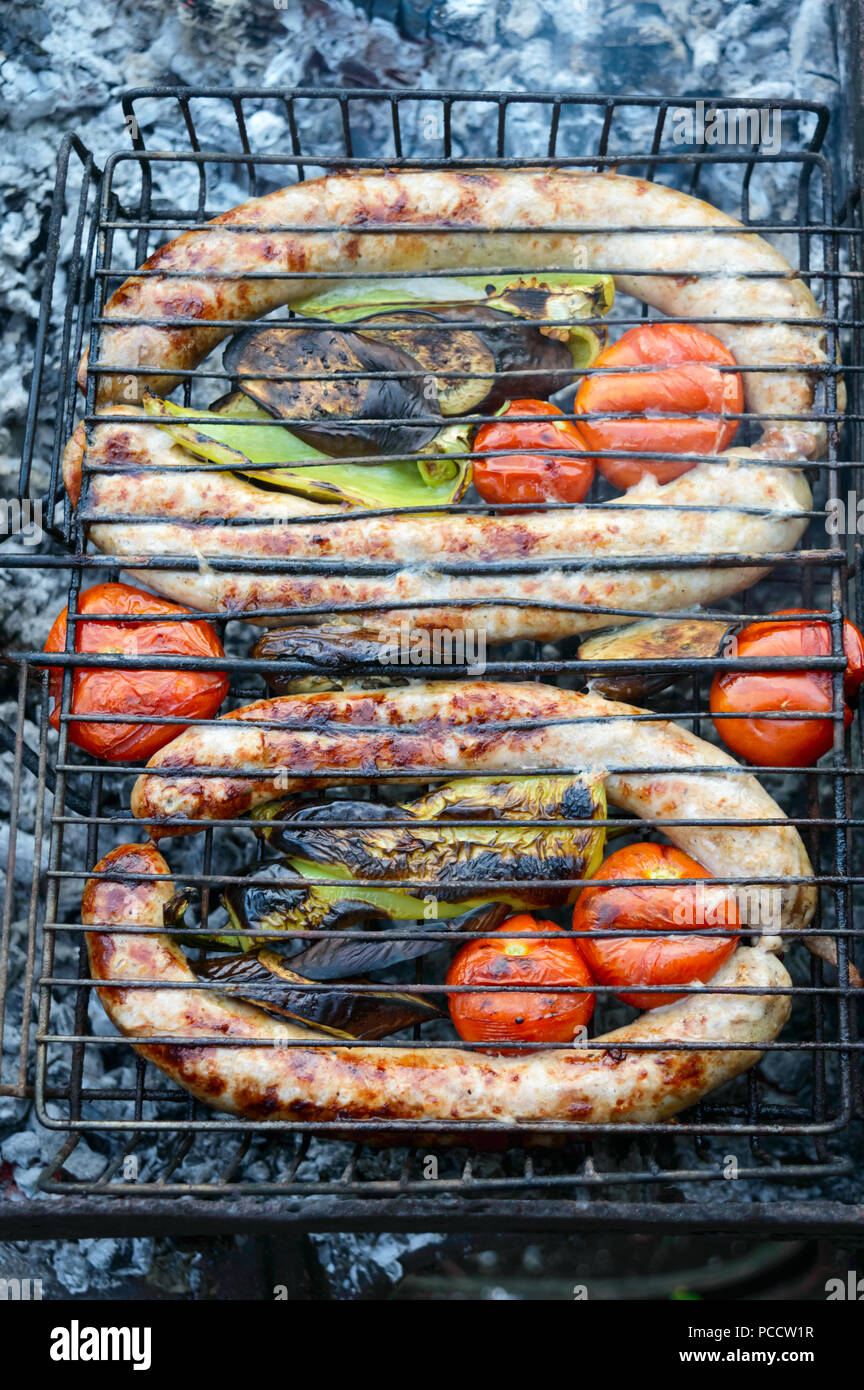 Pork sausages with vegetables are grilled on fire. Cooking dinner ...