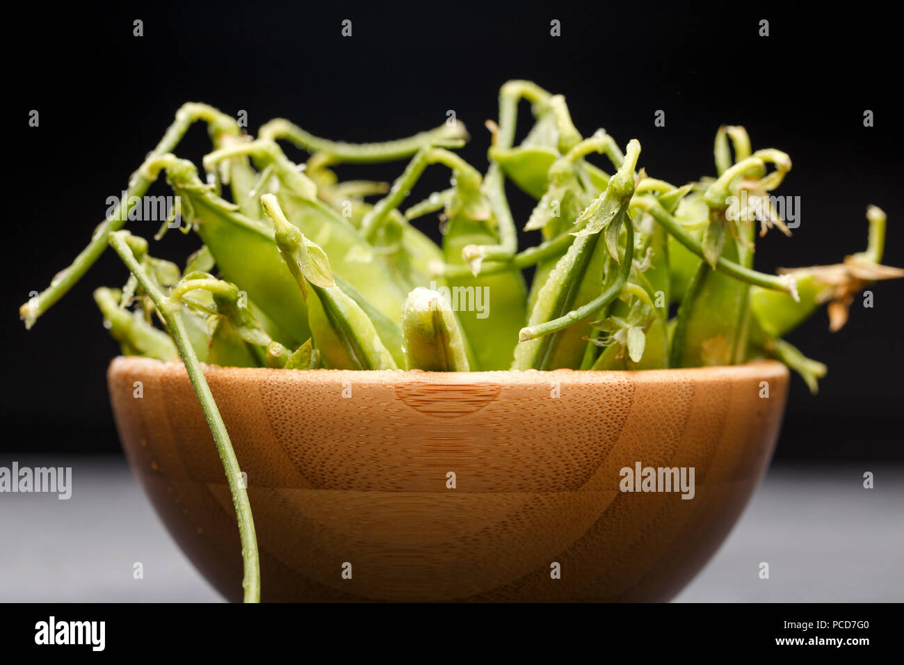 Photo of green pea pods in wooden cup on blank black background in ...