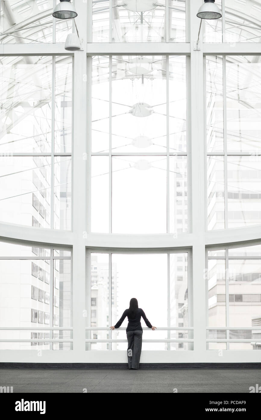 A businesswoman standing at a window in a large convention center lobby ...
