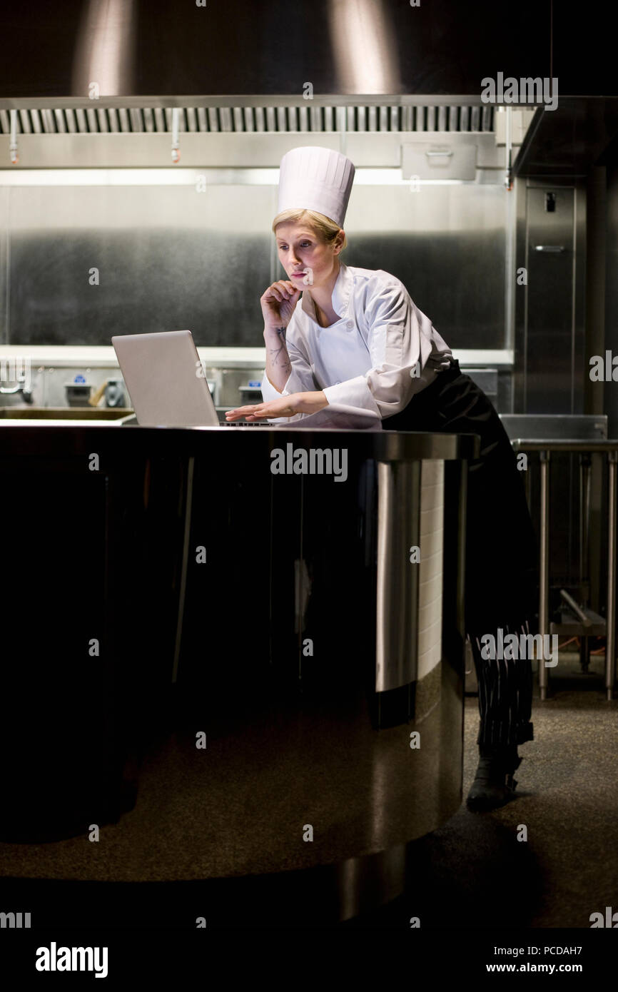 A caucasian female chef working on a laptop computer after hours in a ...