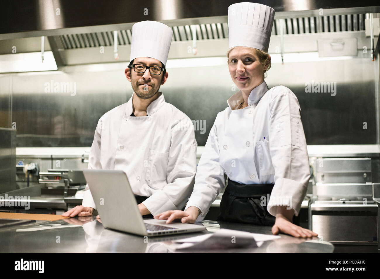 A portrait of a mixed race pair of chefs working with a laptop computer ...