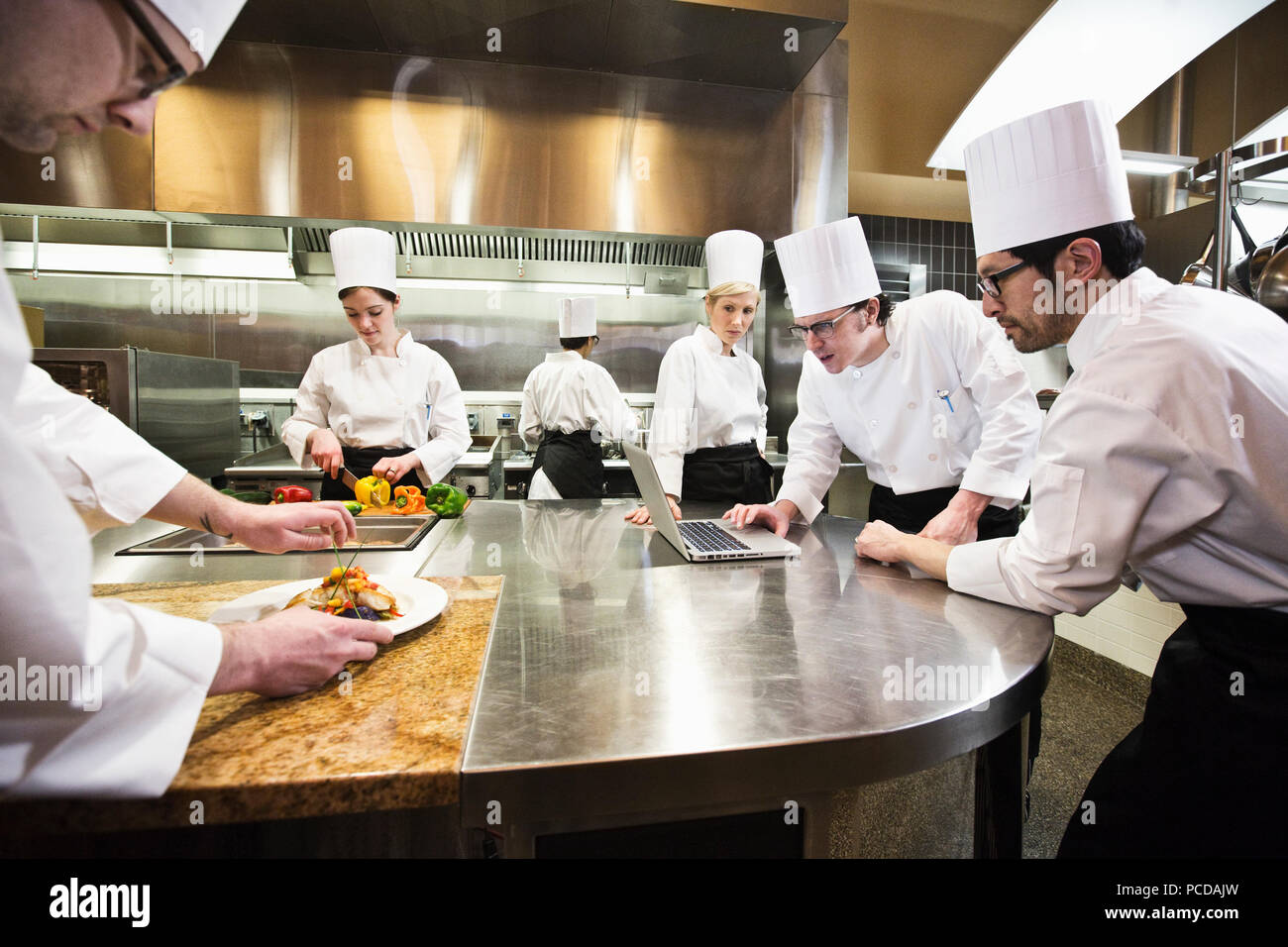 A crew of chef's working in a commercial kitchen, while several chefs ...