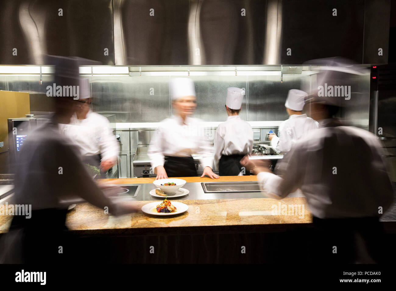 A blurred view of a crew of chefs working around a commercial kitchen ...