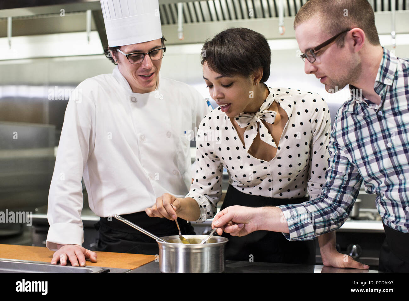 A caucaisan male chef teaching a cooking class for a mixed race grop of ...