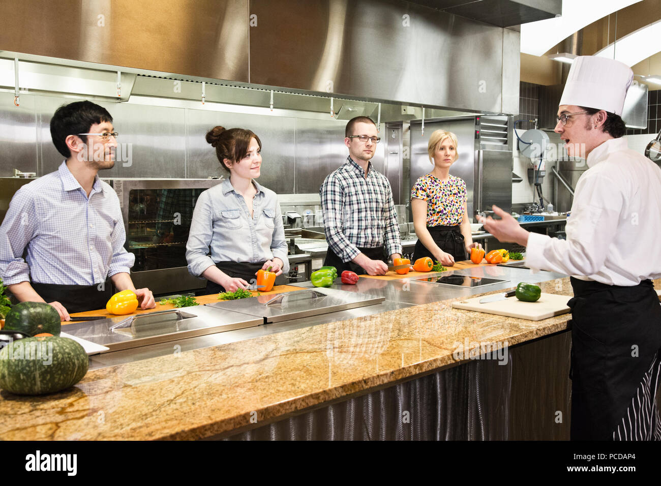 A caucaisan male chef teaching a cooking class for a mixed race grop of ...