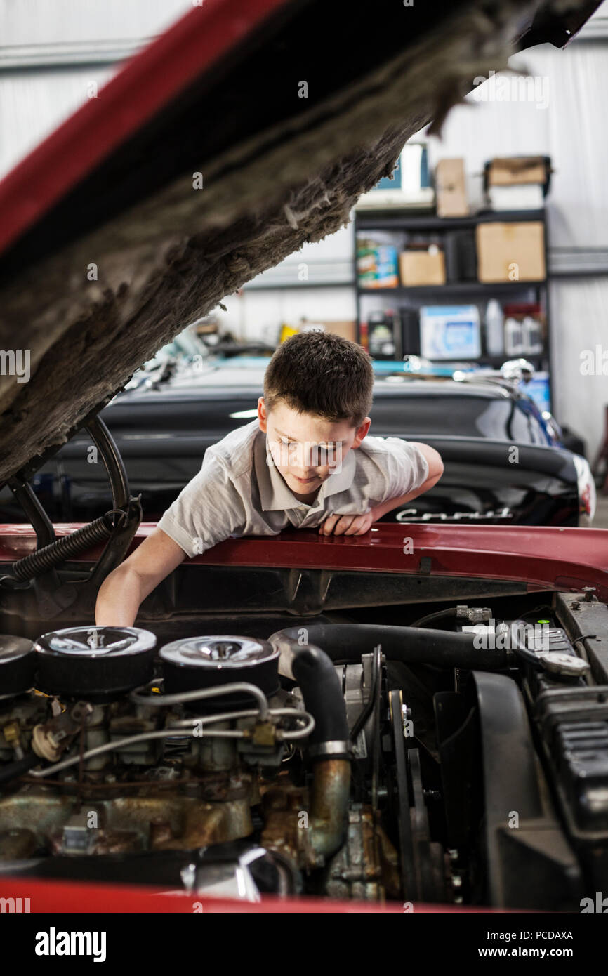 A young caucasian boy checking out an engine in his father's classic ...
