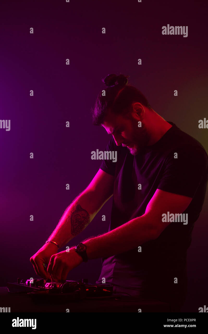 Attractive young DJ playing on turntables with color light effects. A ...