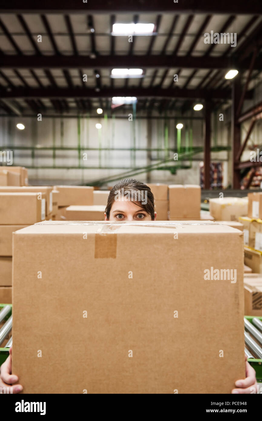 A caucasian female warehouse worker behind a cardboard box in a ...