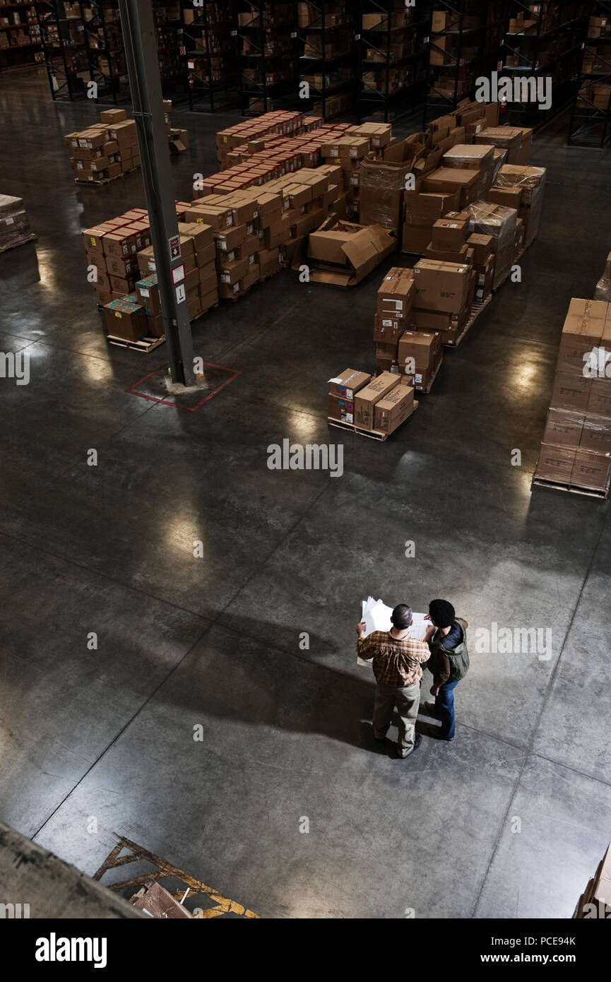 Two warehouse workers going over inventory sheets of products in a ...