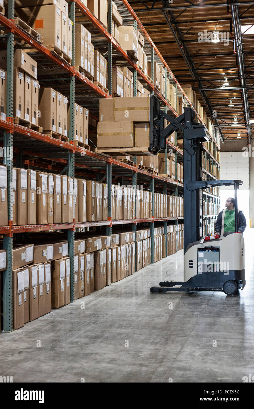 An employee picking products off a rack using a forklift stock picker ...