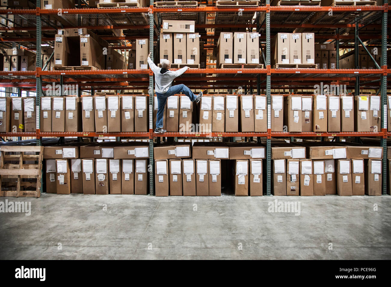A warehouse worker trying to climb a rack of products in a distribution ...