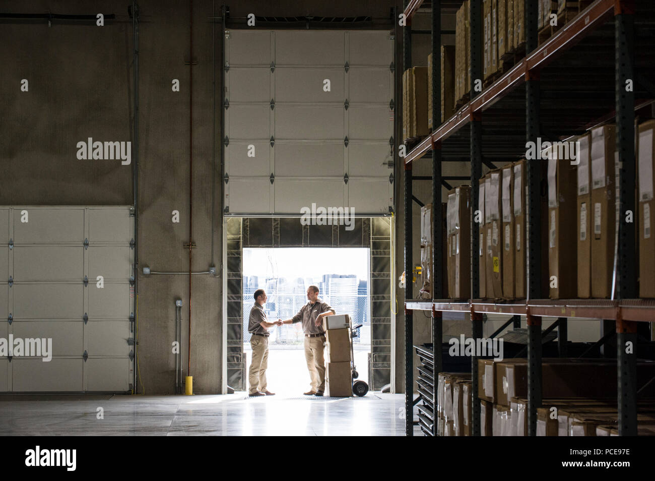 Two warehouseworkers shaking hands while standing in the doorway of a ...
