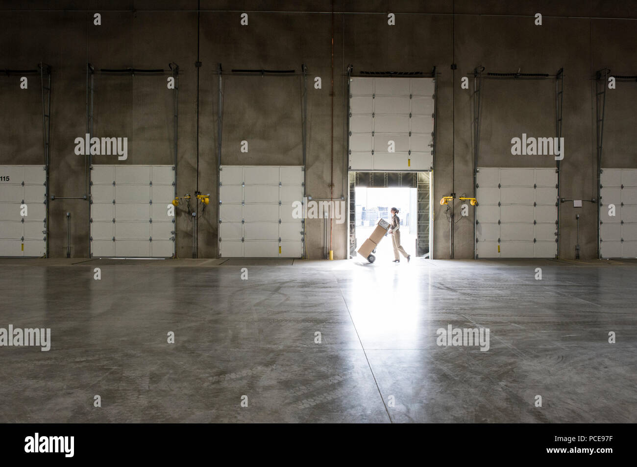 A warehouse worker with a hand truck walking past an open loading dock ...