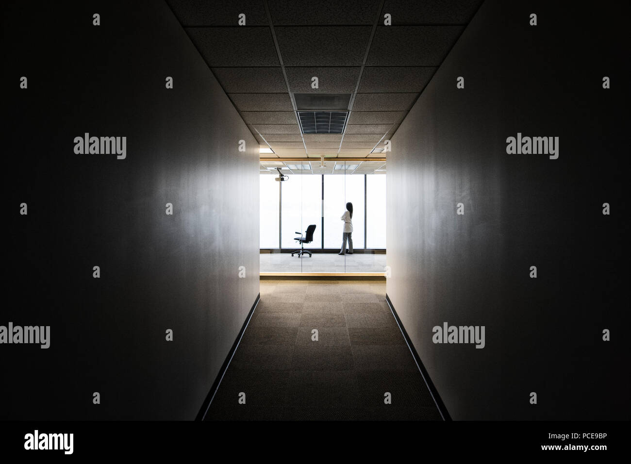 A businesswoman standing at a window at the end of a long hallway Stock ...