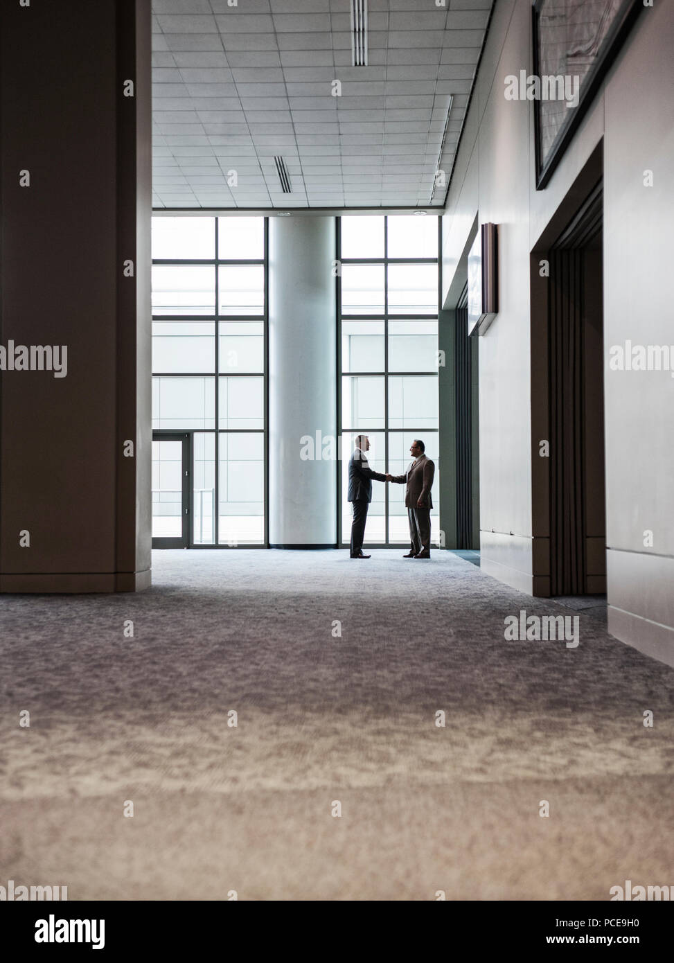 Two businessmen silhouetted and shaking hands in front of a large ...