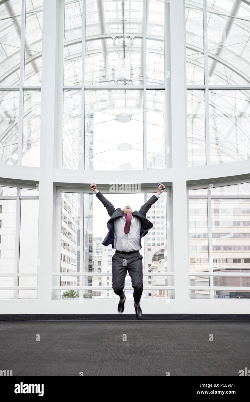 A businessman jumping for joy in front of a large window in a ...