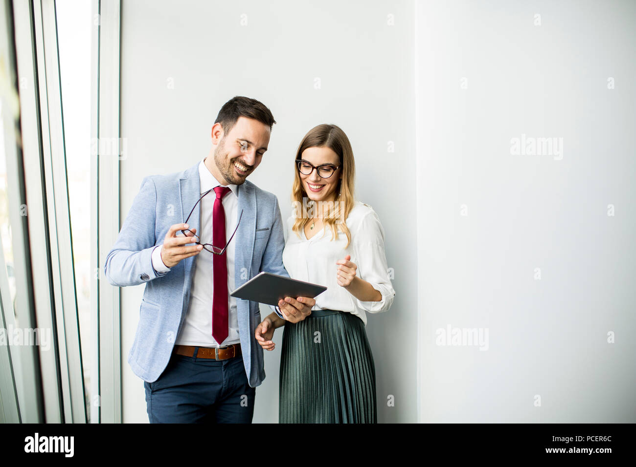 Happy business colleagues in modern office using tablet against wall ...