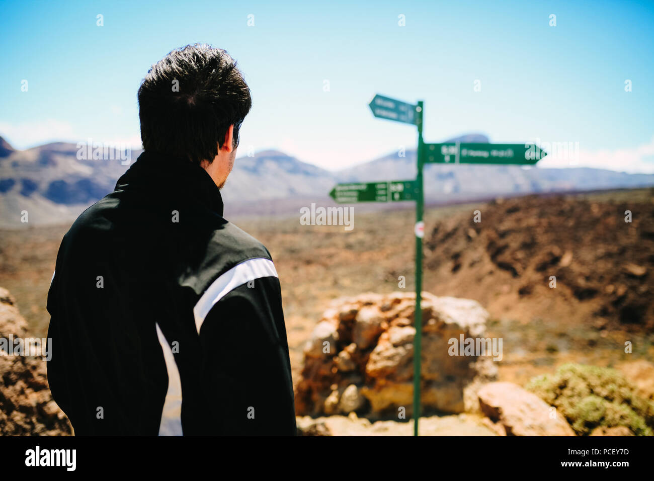 Young man looking in the crossroad sign on the hiking path Stock Photo ...