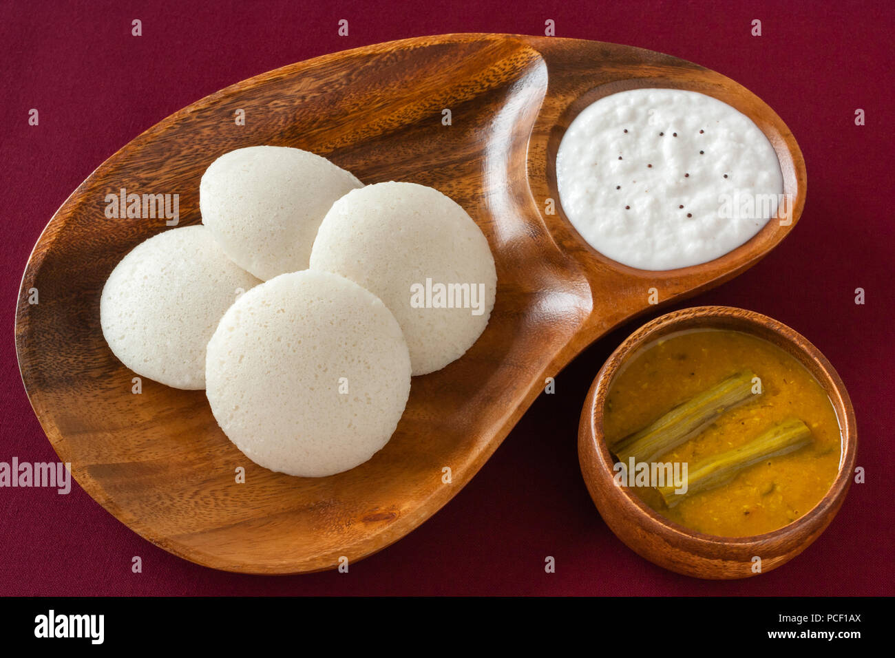 Fresh steamed Indian Idly (Idli / rice cake) arranged on a wooden plate ...