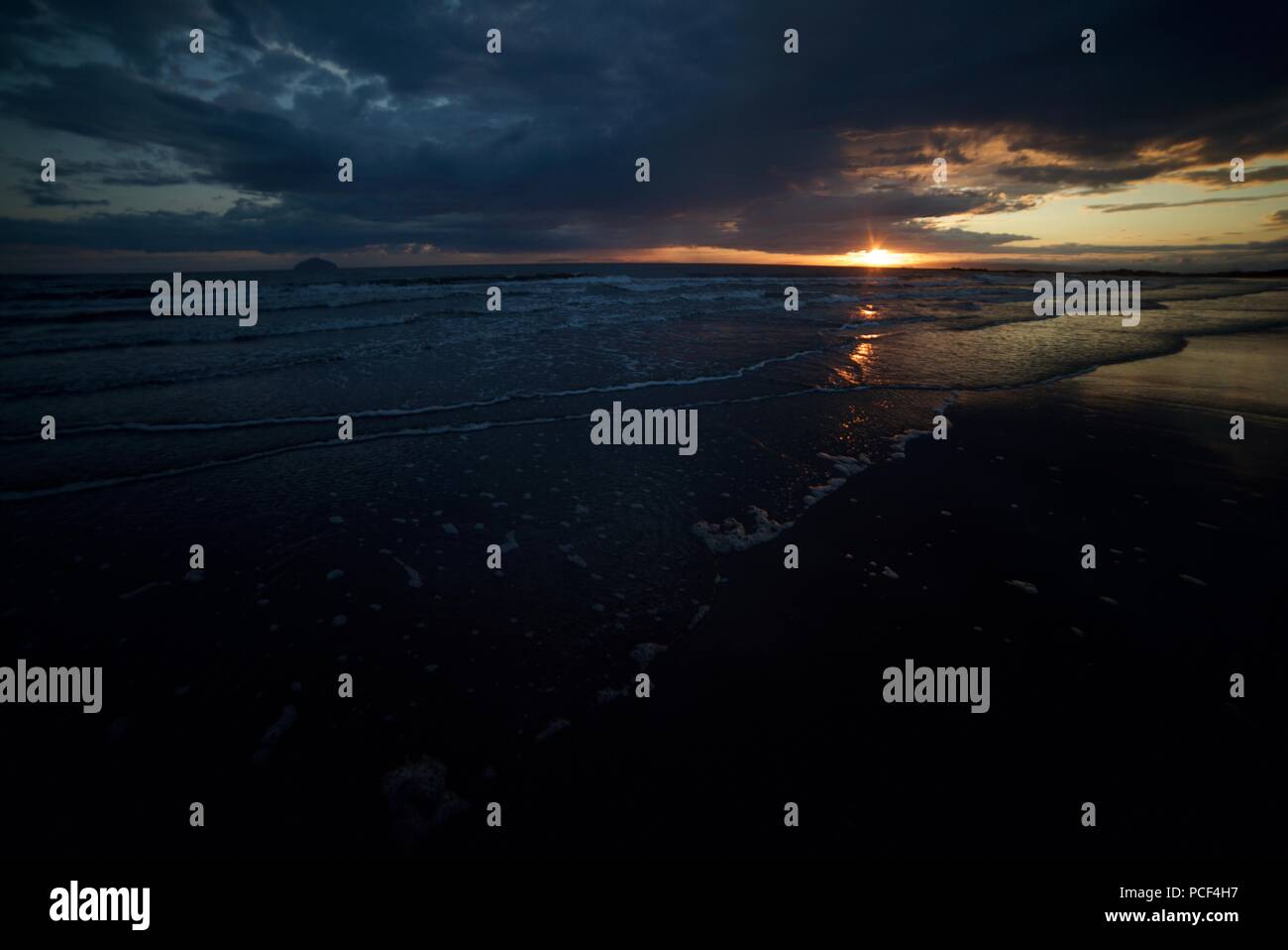 Sun reflecting on water during a beautiful orange sunset at a sandy ...