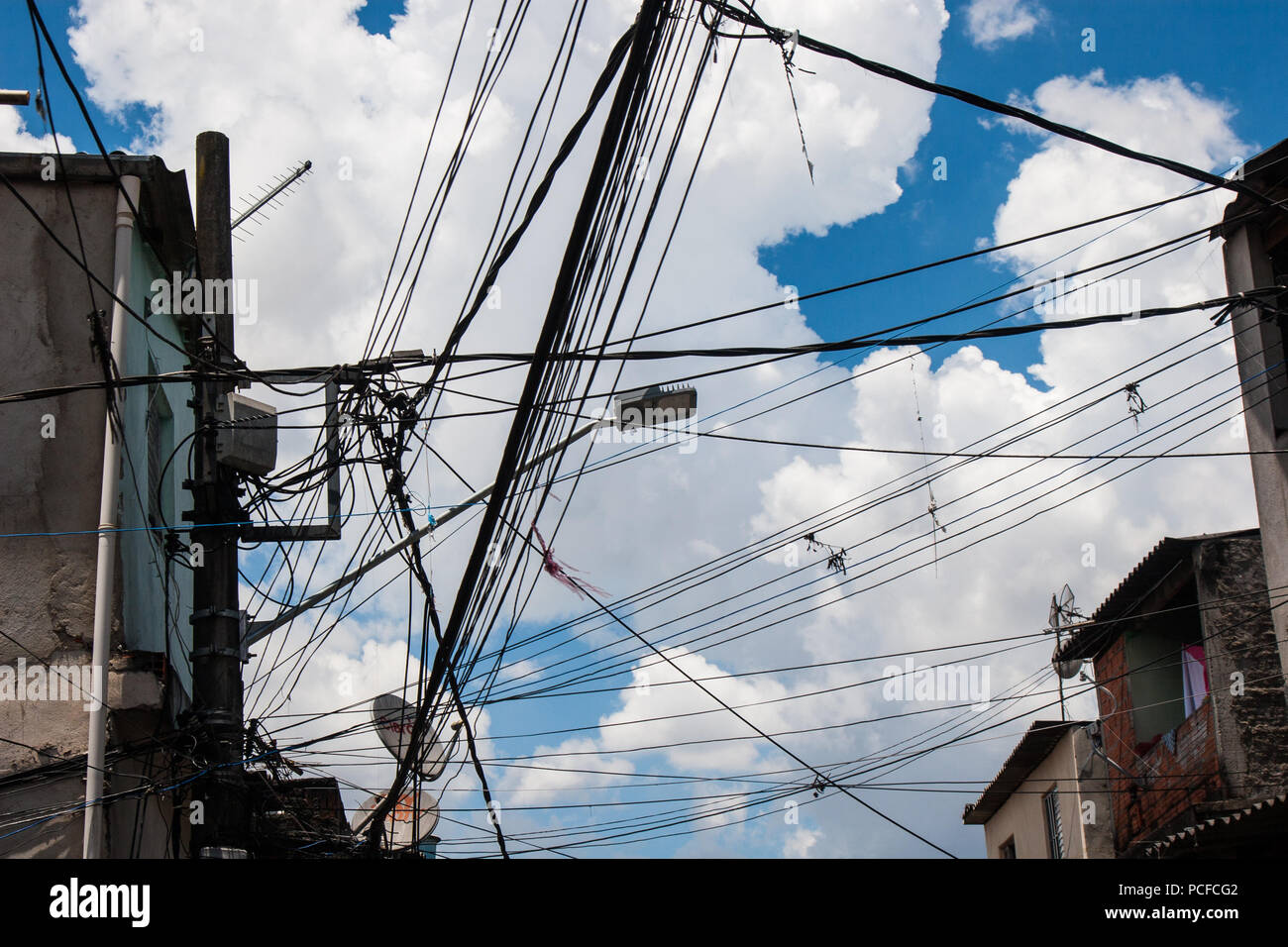 Electric and tv wires in a slum with blue sky and clouds background ...