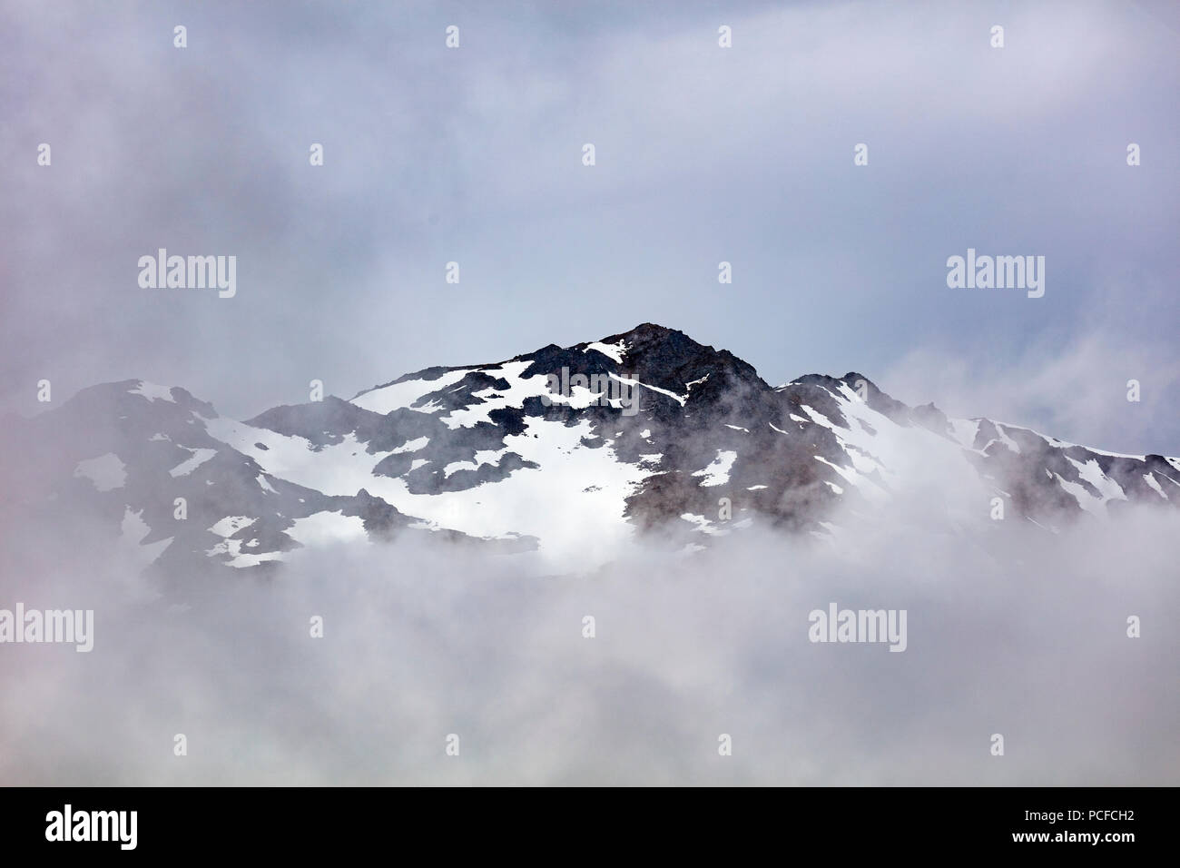 Snow capped rugged rocky mountains in clouds on the Kenai Peninsula of ...