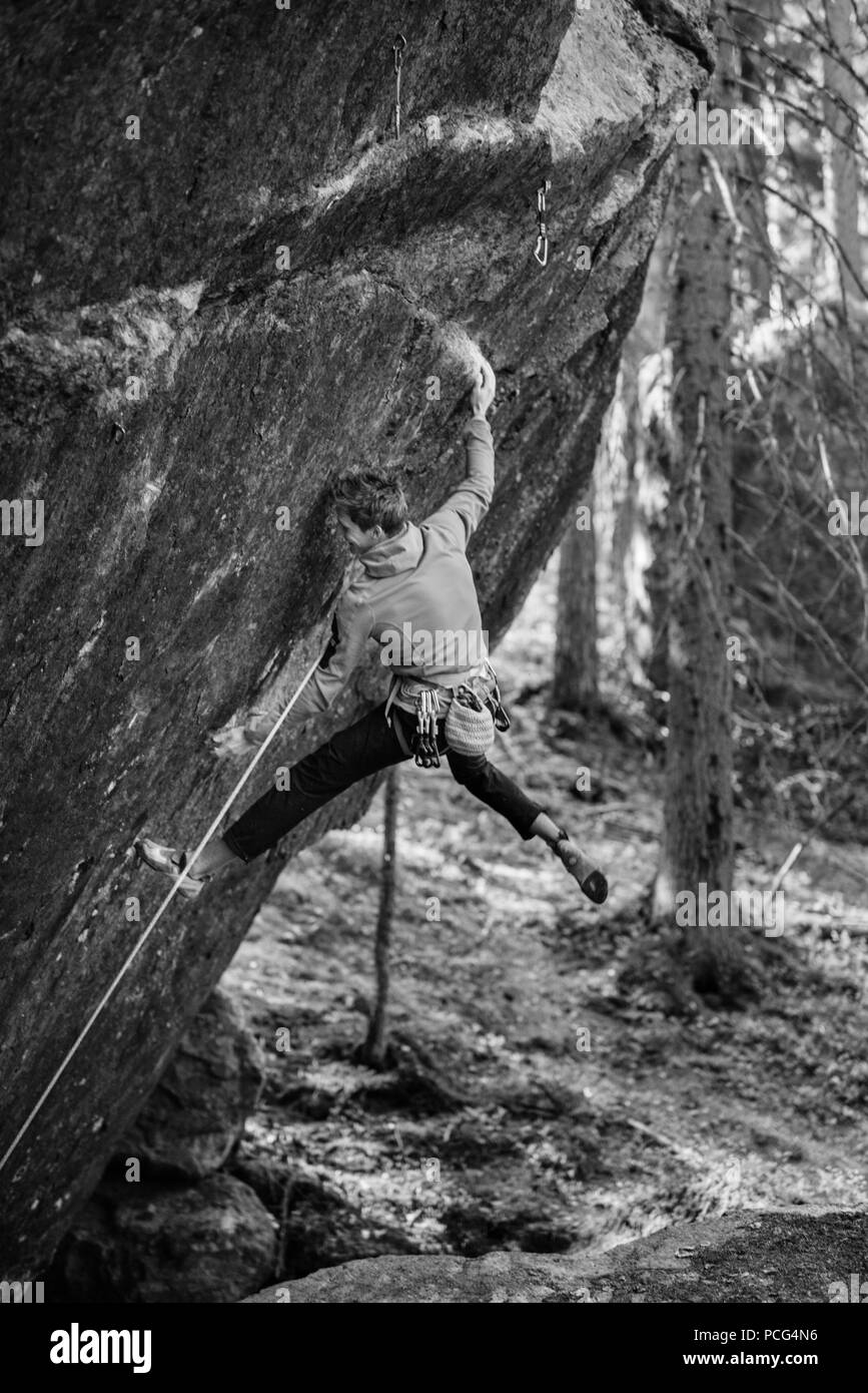 Young climber man climbing a rock in scandinavian forest. Northern ...