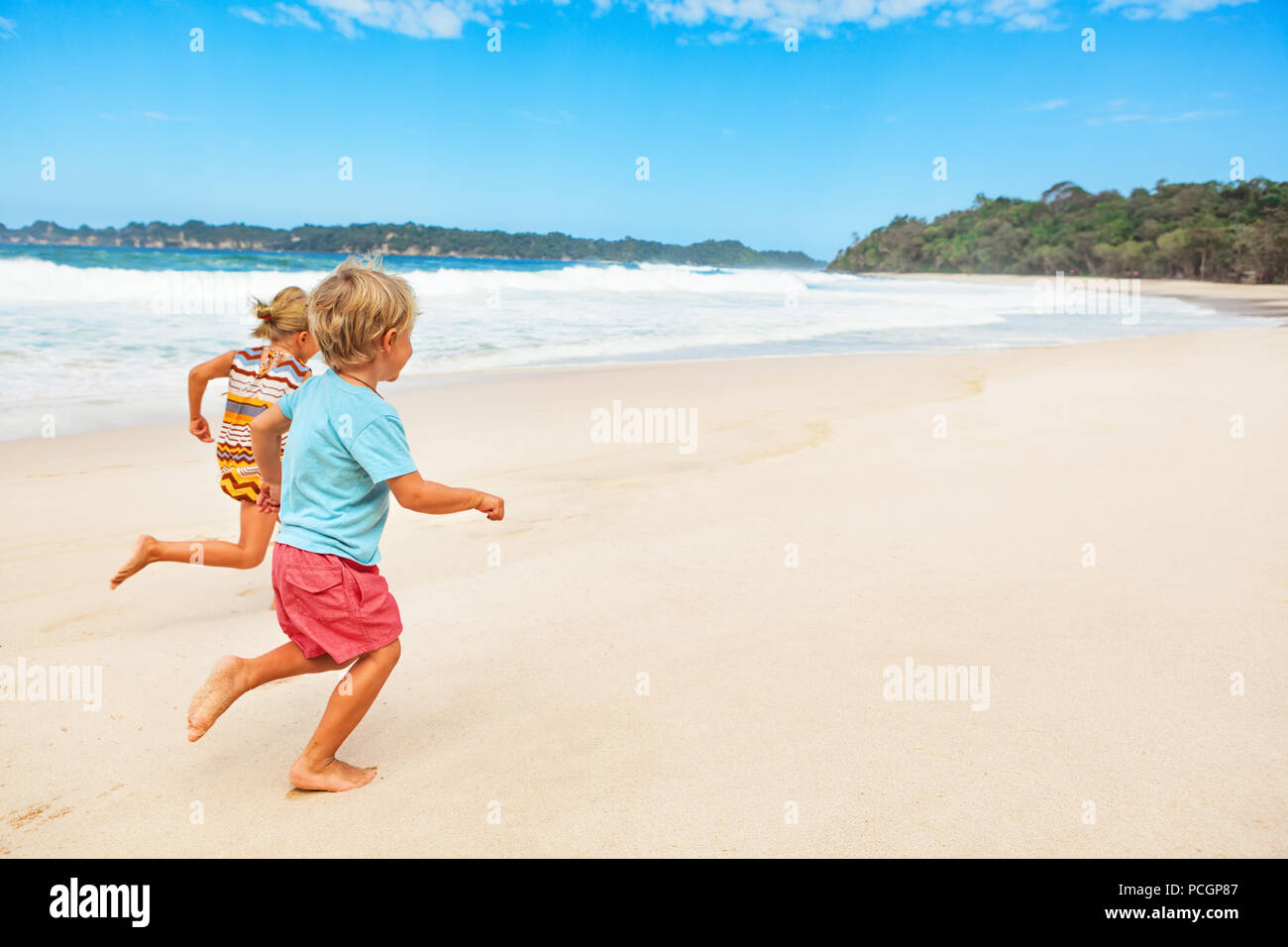 Happy barefoot kids have fun on beach walk. Run and jump by white sand ...