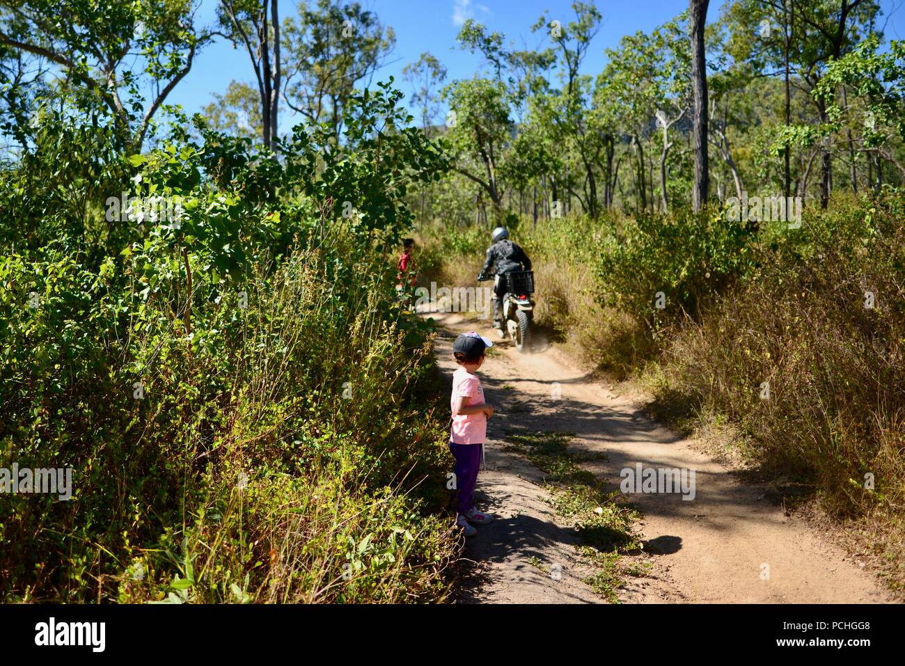 A motorbike rider passes a child on a dry dusty dirt track in the ...
