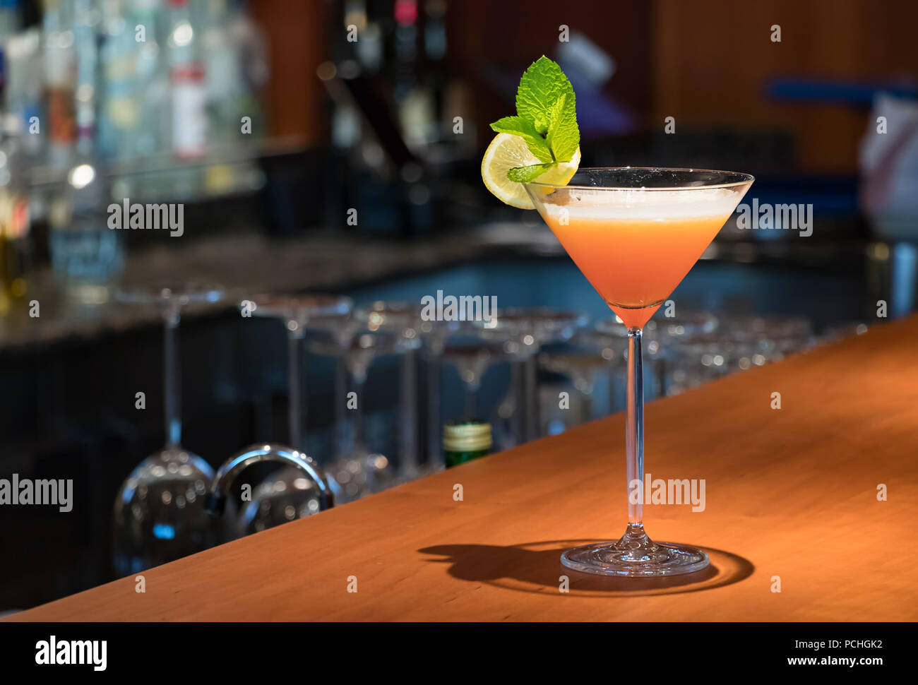 An orange color martini drink on a transparent glass with a lime slice ...