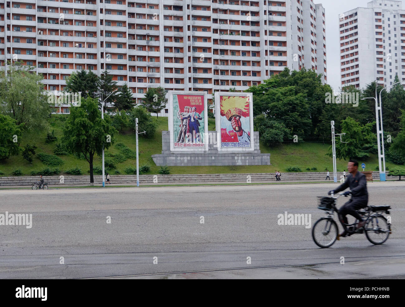 Cyclist passes the inspiration posters that abound in Pyongyang streets ...