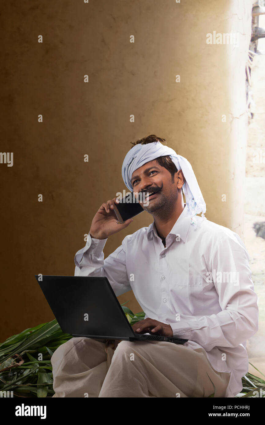 Rural man talking on phone while working on laptop Stock Photo - Alamy