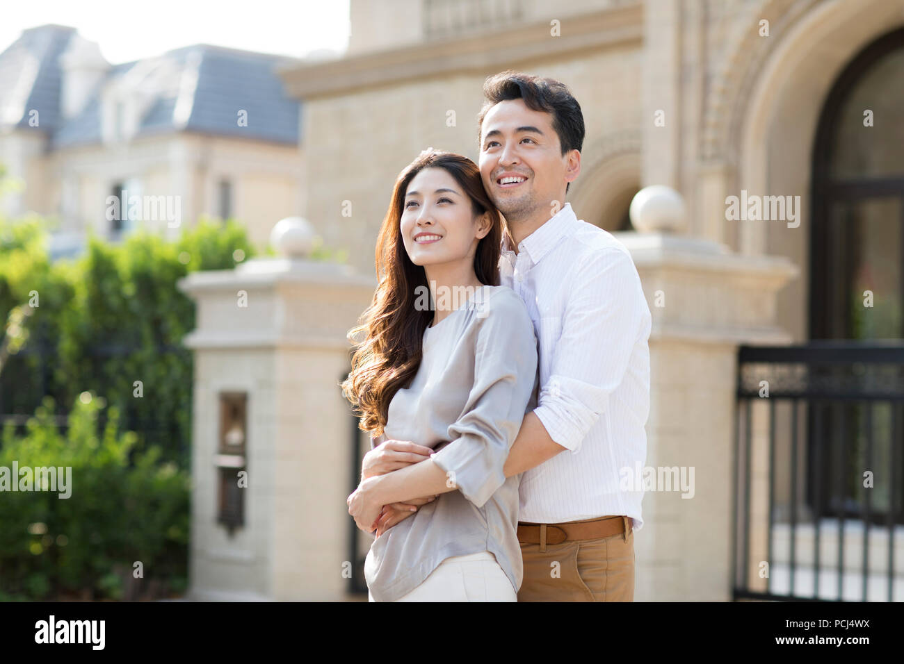 Cheerful young Chinese couple embracing in front of their villa Stock ...