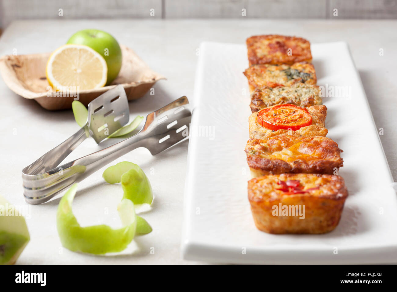Individual mini quiches on a white rectangular plate with tongs apple ...
