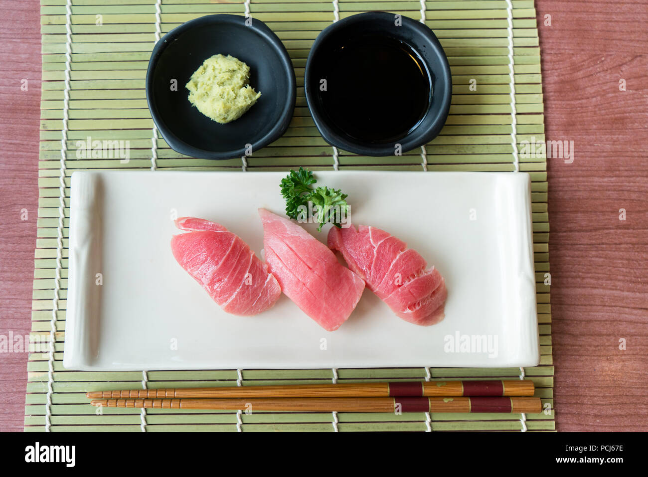 Otoro tuna sushi on black plate along with Japanese sauce and green ...