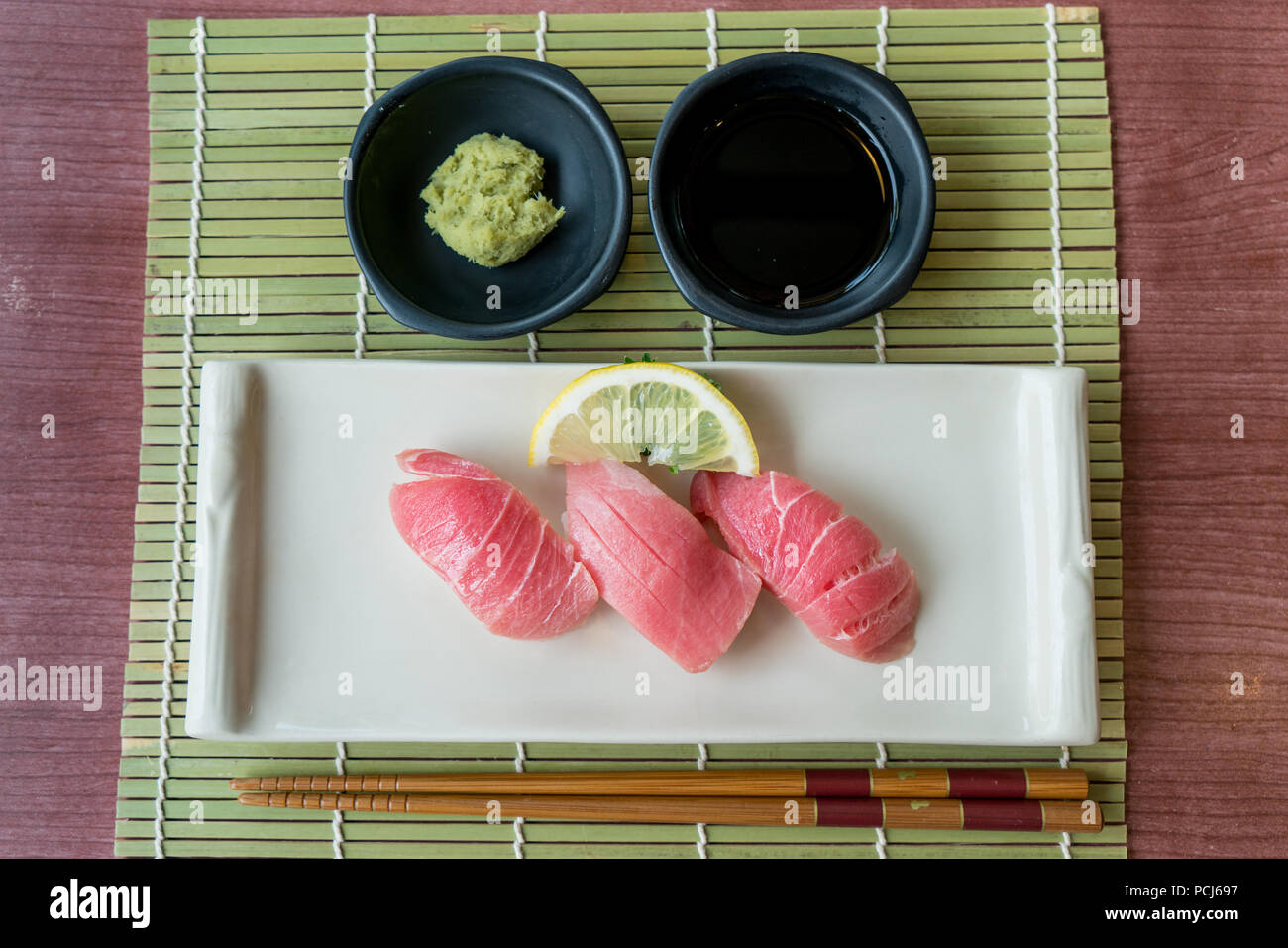 Otoro tuna sushi on black plate along with Japanese sauce and green ...