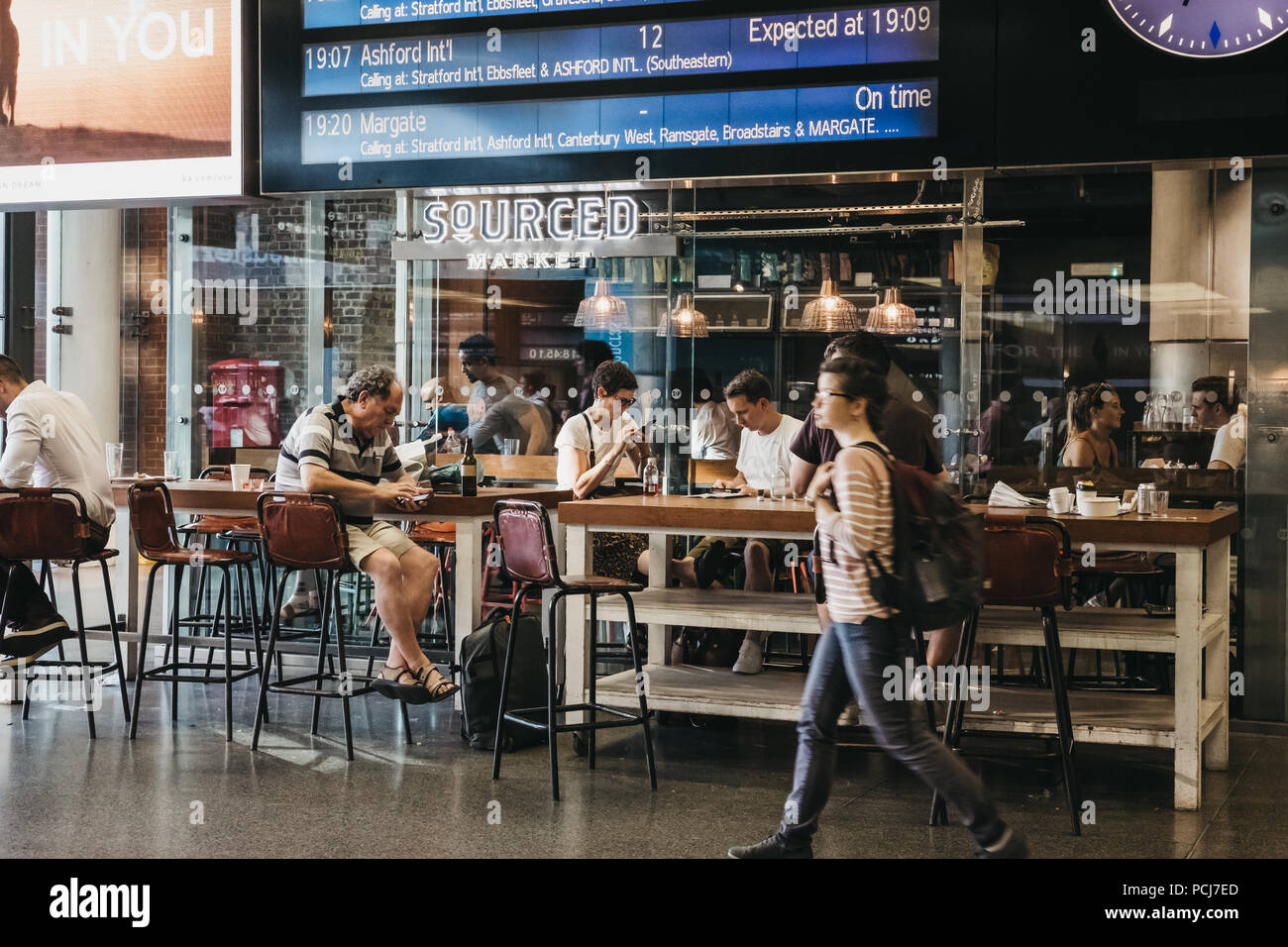 People sitting at a cafe, waiting for their trains under the departure ...