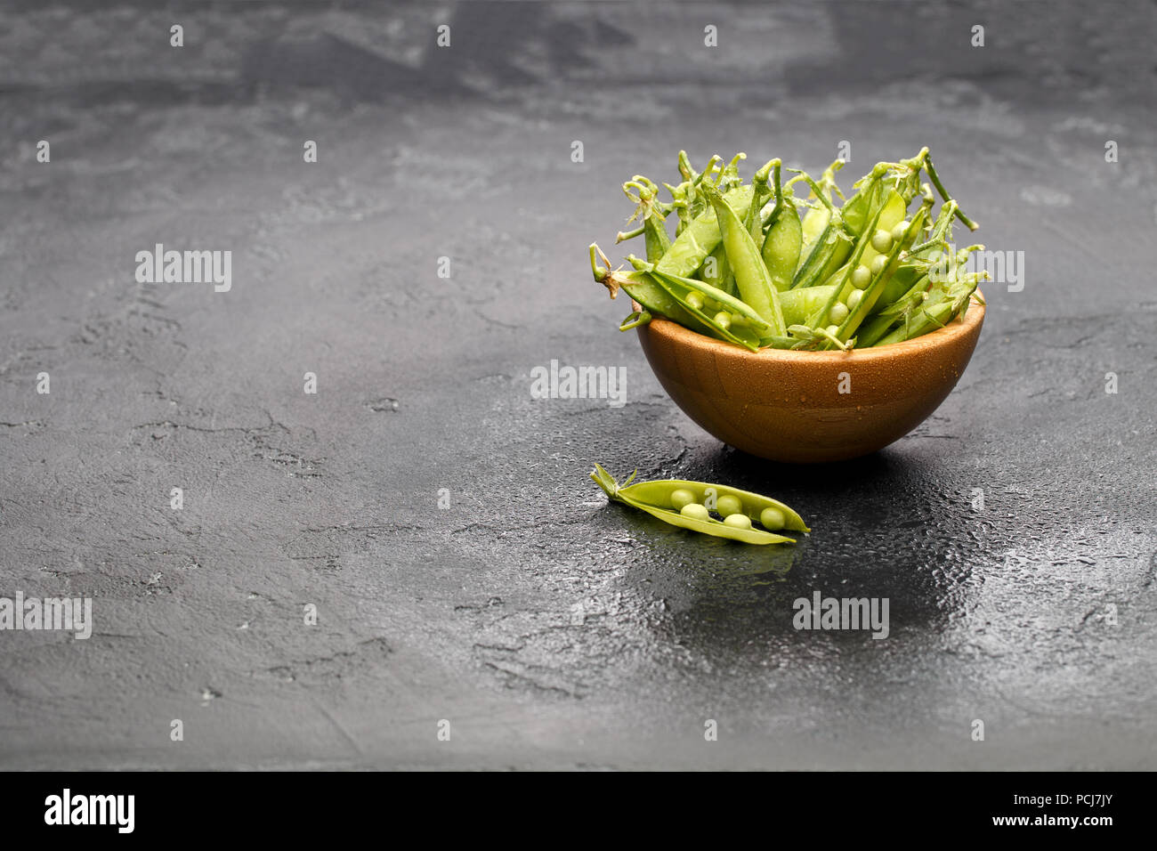 Photo of green pea pods in wooden plate on blank black table with pod ...