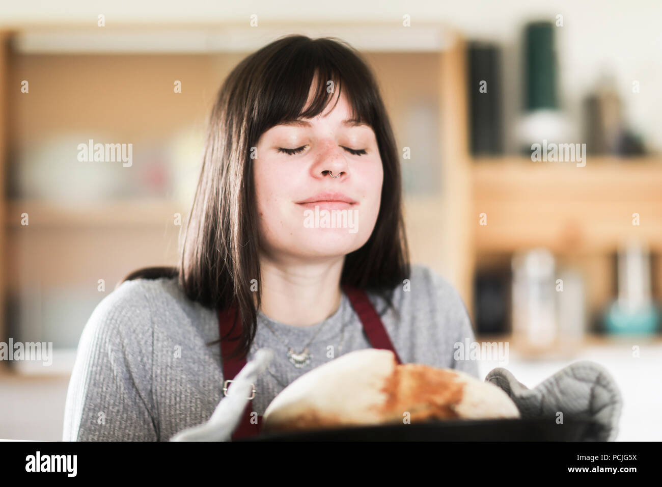 Smiling Woman standing in the kitchen holding a freshly baked loaf of ...