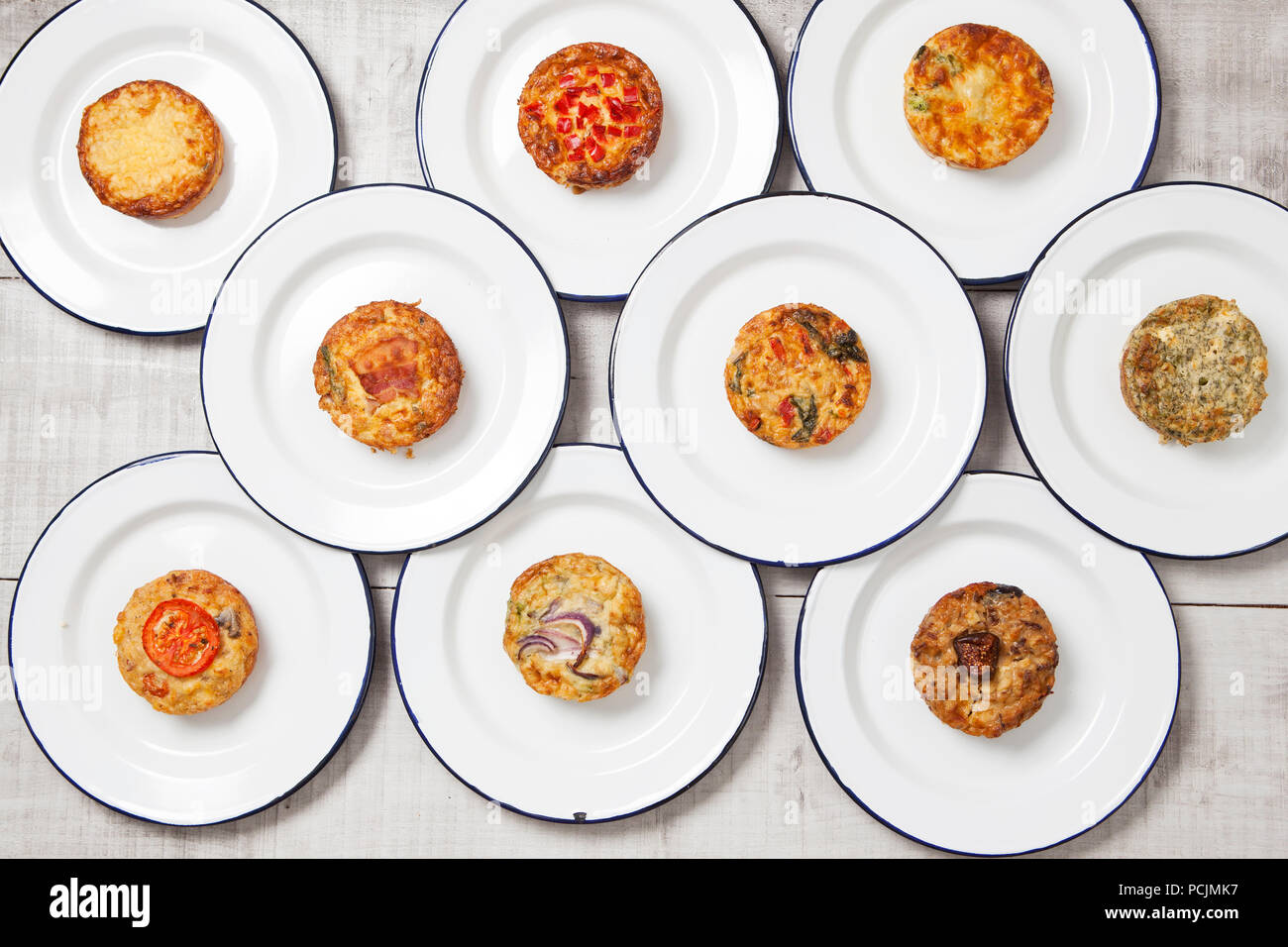 Mini individual quiches on white enamel plates on a light wooden table ...
