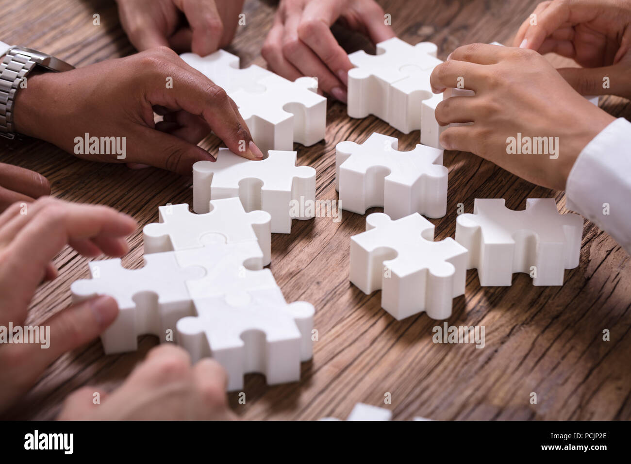 Businesspeople Solving White Jigsaw Puzzle Together On Wooden Desk ...